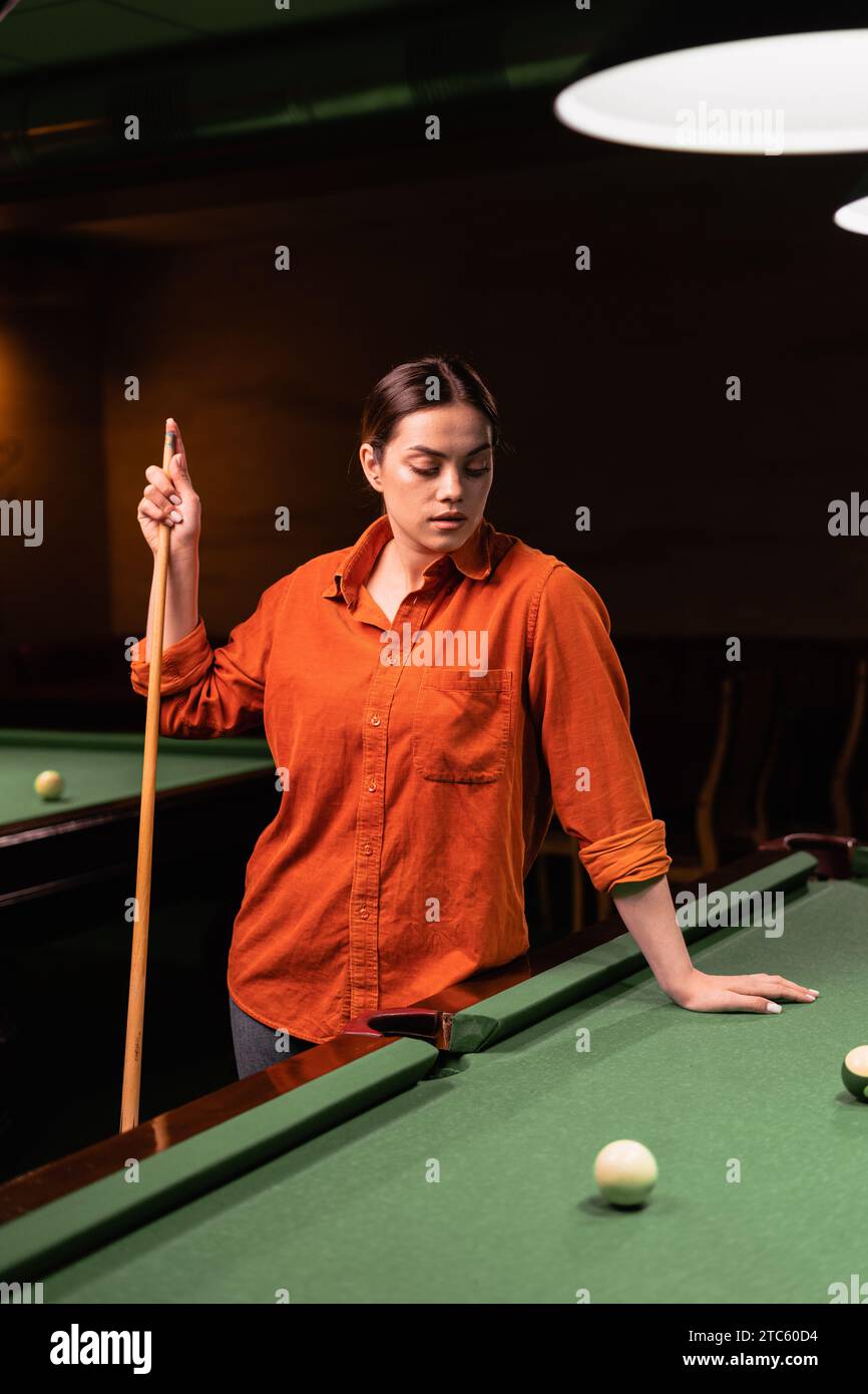 Beautiful woman standing near a pool table with a cue in her hands ...