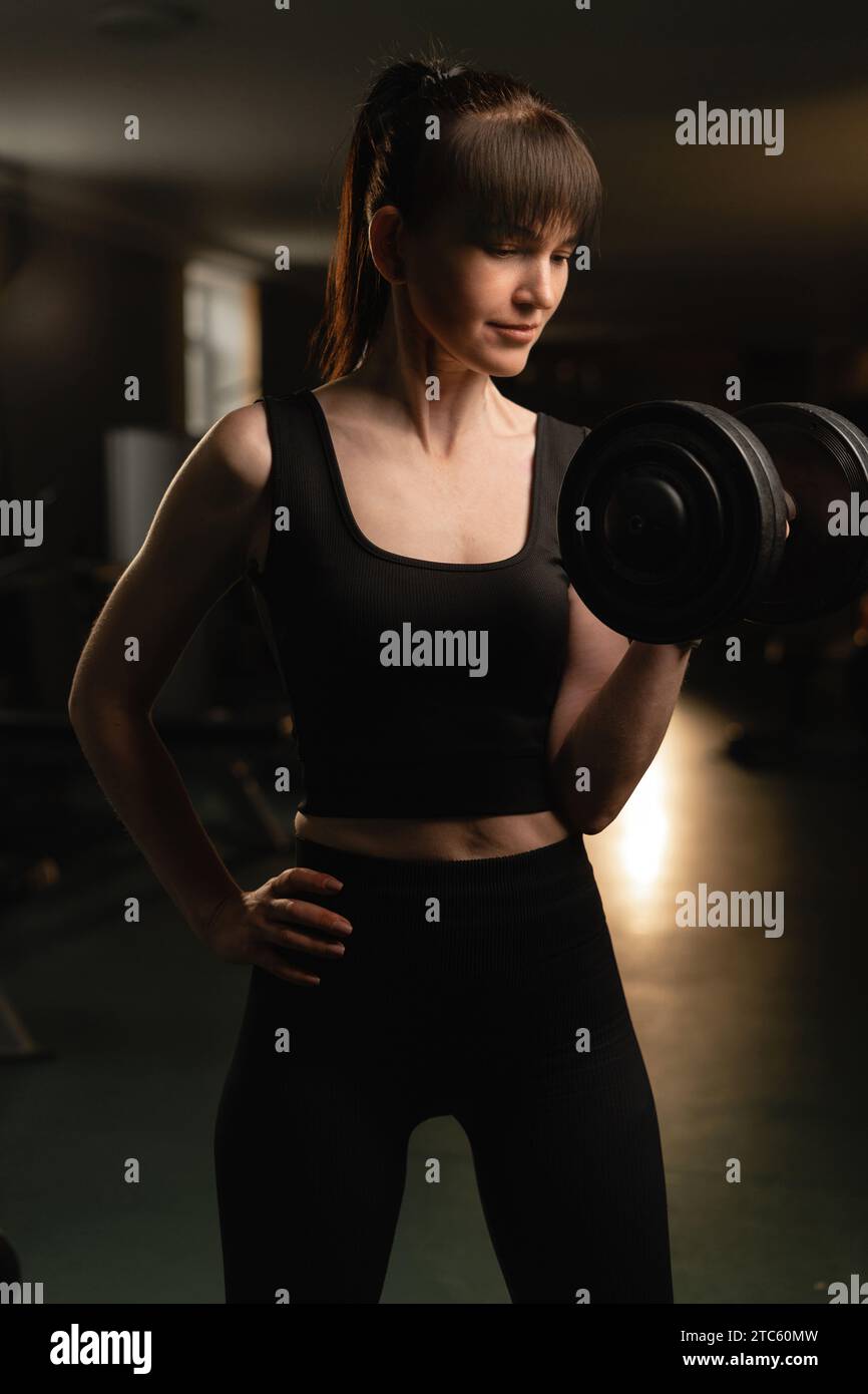Focused female athlete exercising with dumbbells for biceps in gym ...