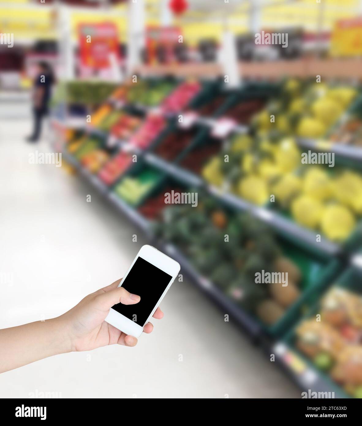 Hand holding mobile phone with Vegetables and fruit on shelf in ...