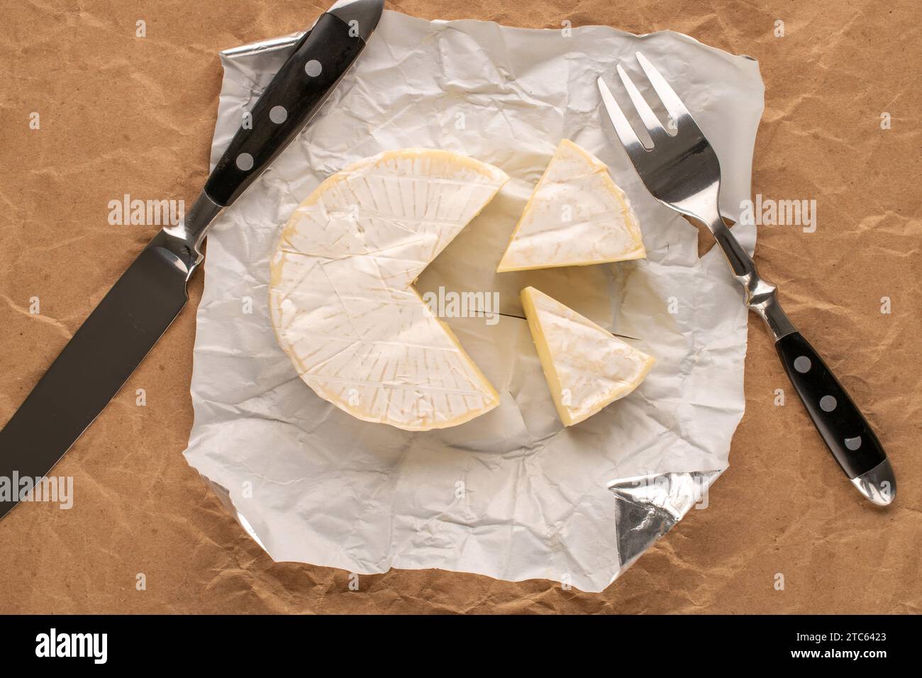 Fragrant brie cheese with paper packaging, knife and fork on kraft ...