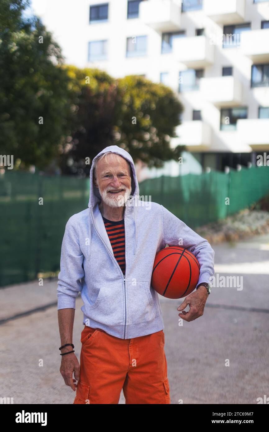 Senior man playing basketball outdoors on basketball court in city ...
