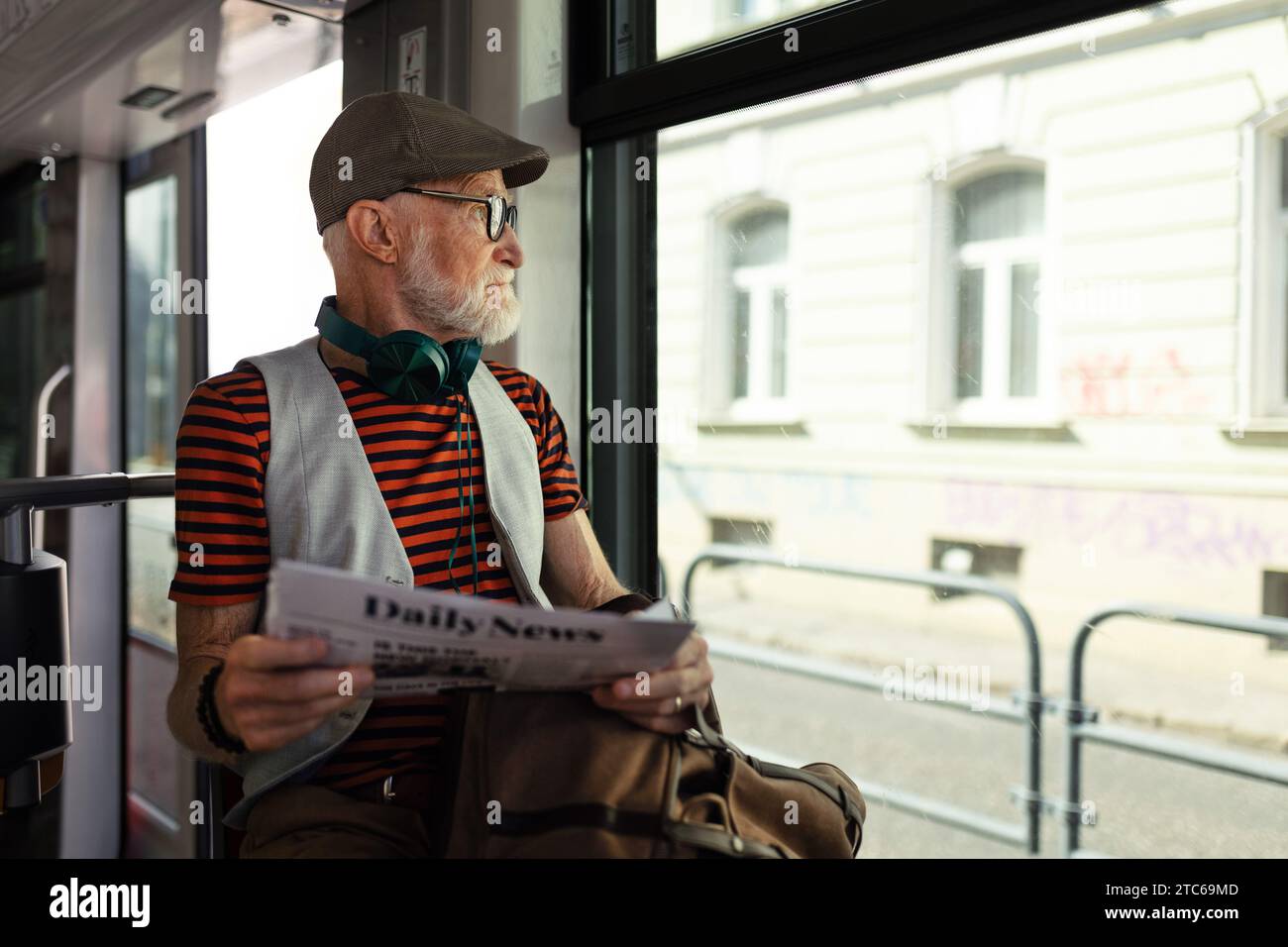 Elderly man traveling through the city by bus, reading newspaper ...