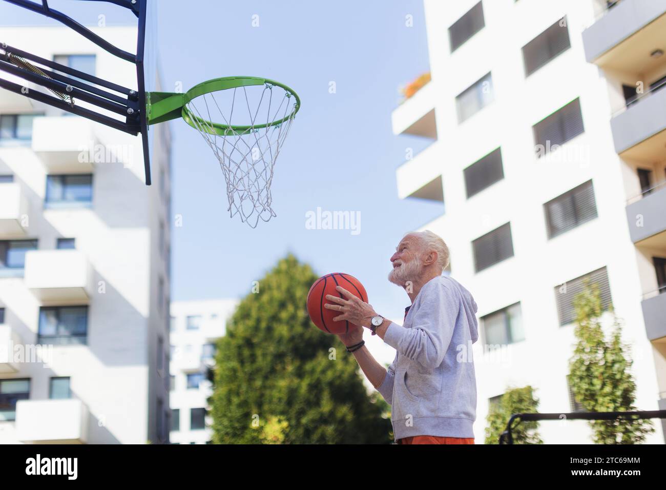 Senior man playing basketball outdoors on basketball court in city ...