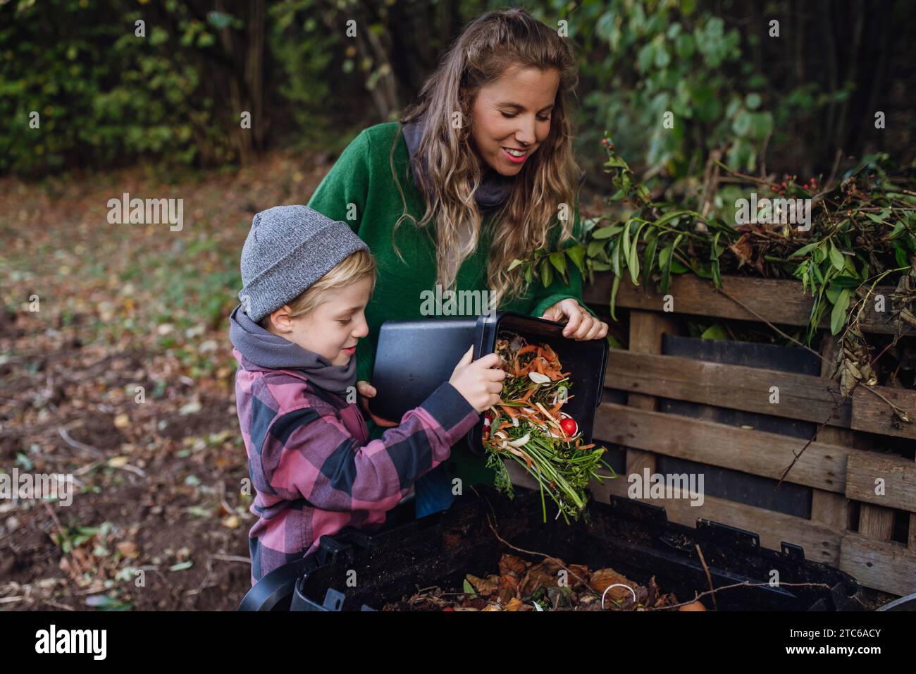 Boy helping mother to put kitchen waste, peel and leftover vegetables ...