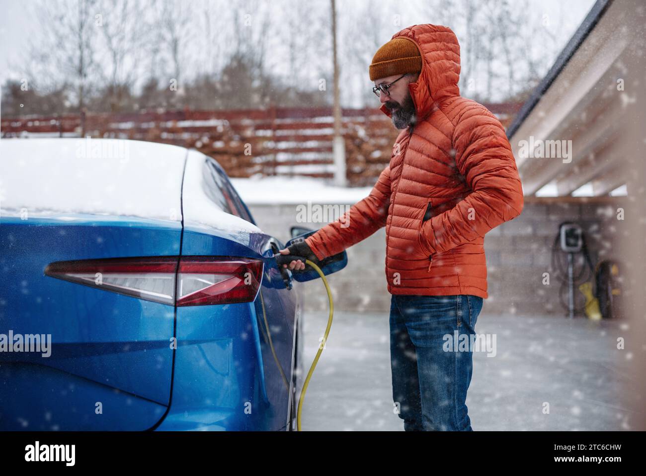 Man charging electric car during cold snowy day. Side view of hansome ...