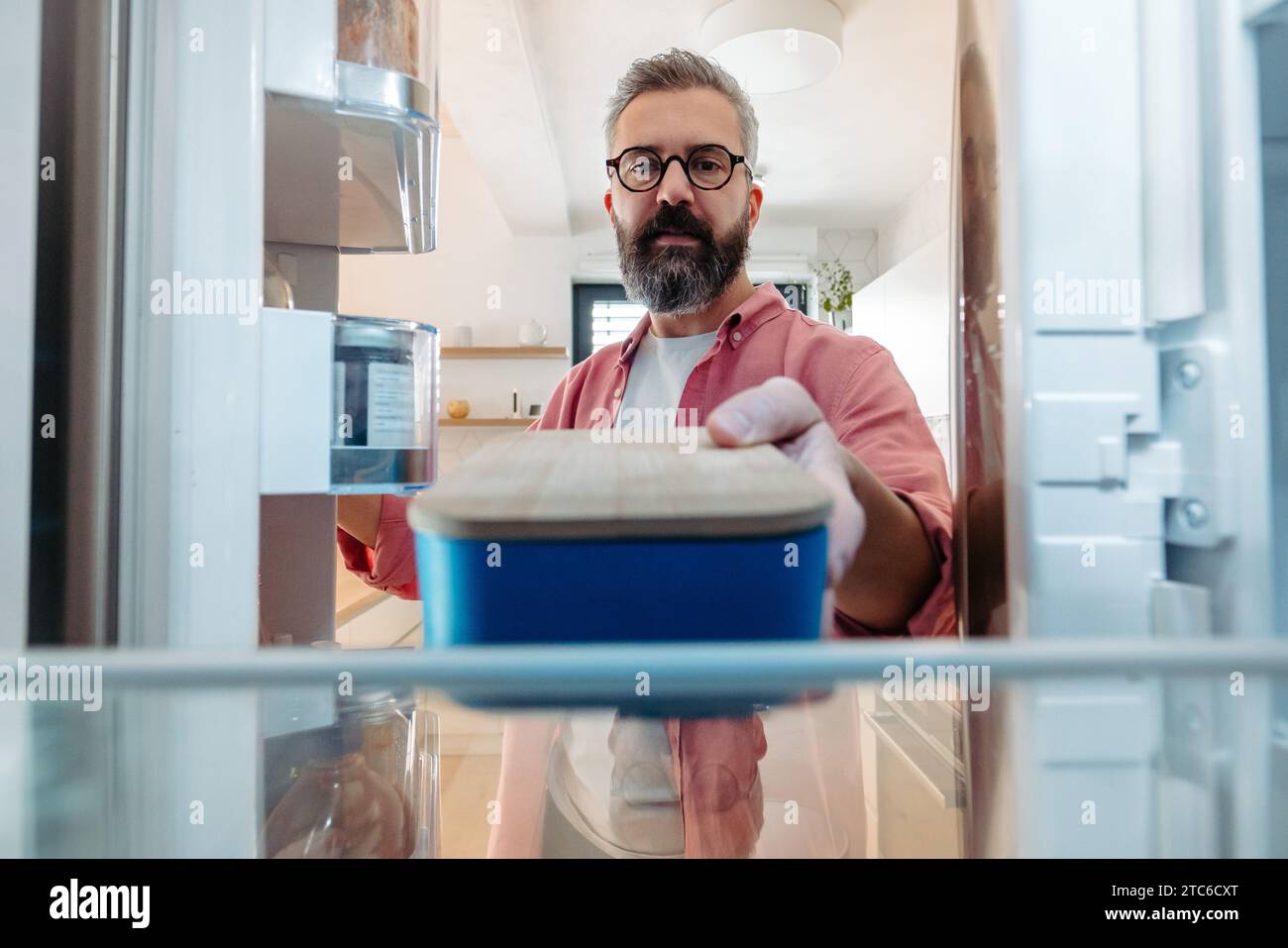 Handsome man putting lunchbox in fridge. Taking out lunch from fridge ...