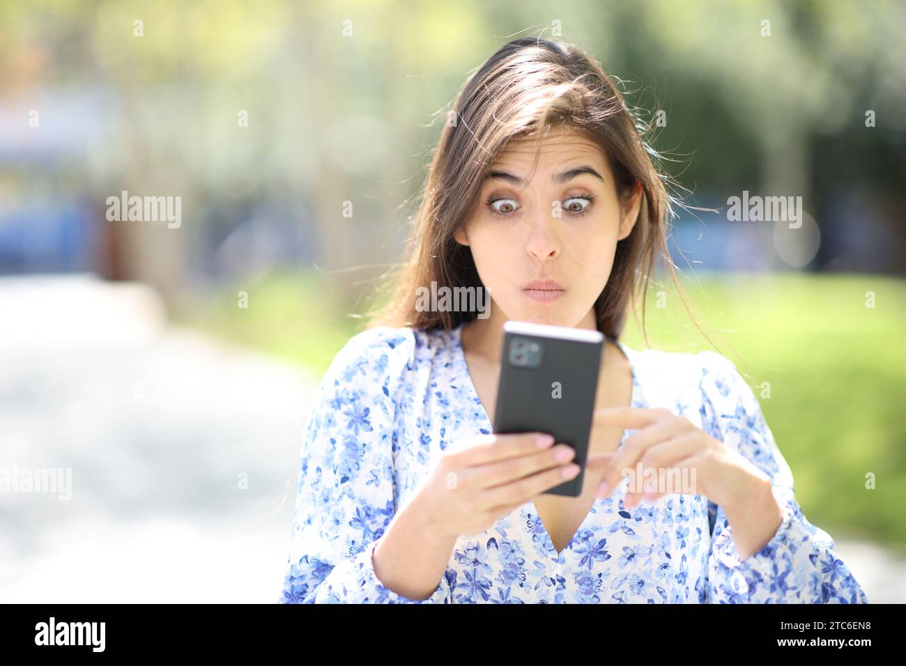 Front view portrait of a perplexed woman checking smart phone outside in the street Stock Photo ...