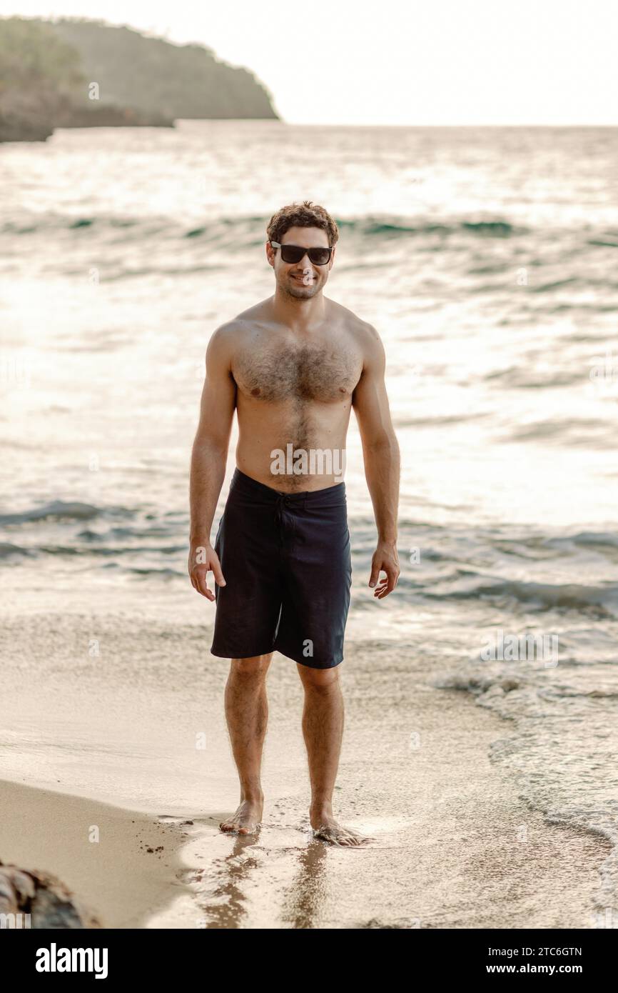 Muscular young man in swim shorts smiles on Dominican beach Stock Photo ...