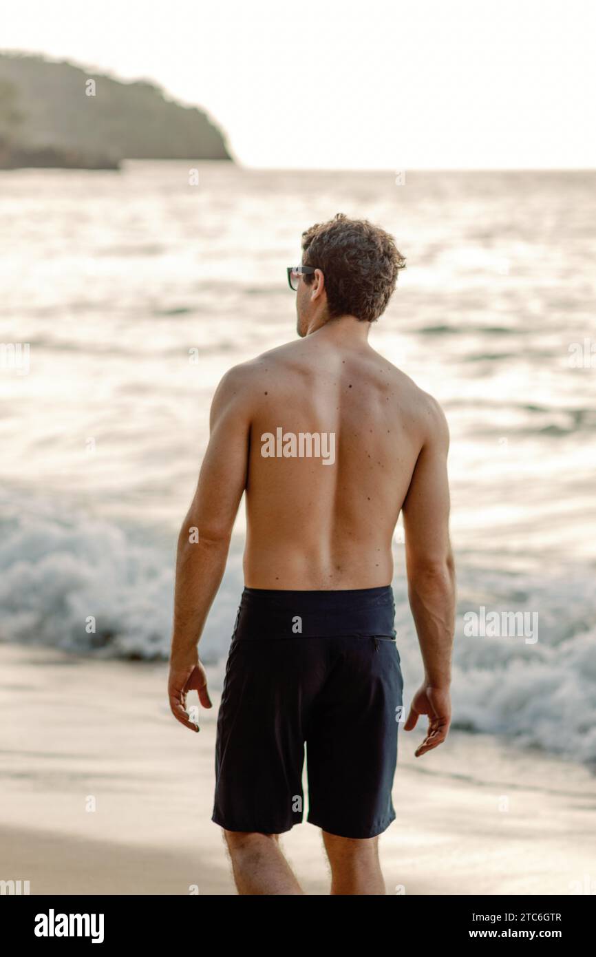 Muscular back, man in swimsuit walks Dominican beach at sunset Stock ...