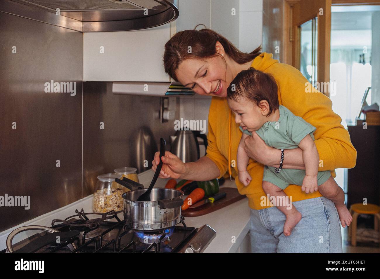 Mom cooks food in the kitchen with a baby in her arms Stock Photo - Alamy