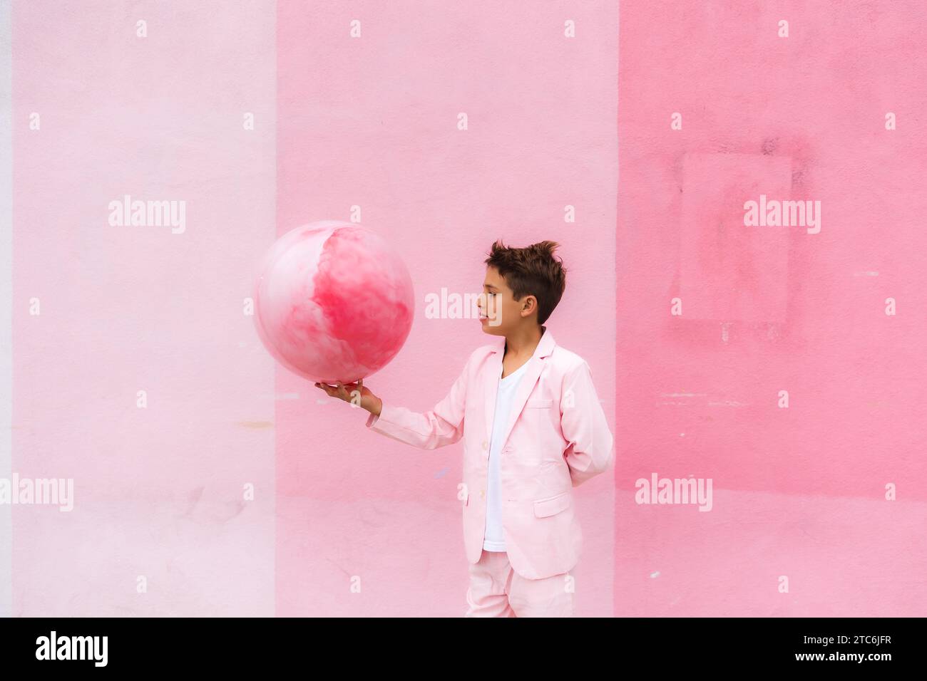 Young boy all pink holding a ball on the sidewalk in a suit Stock Photo ...