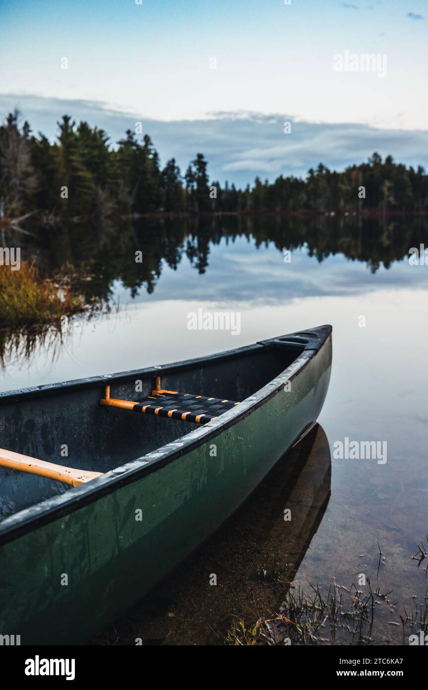 Green canoe sits on the edge of tranquil pond in the Maine woods Stock ...