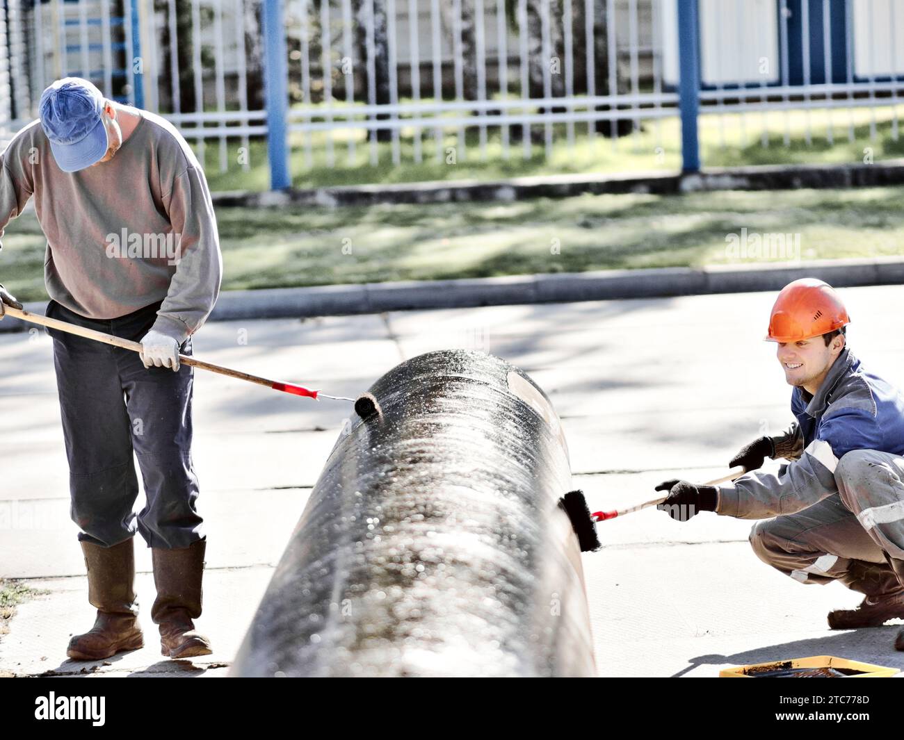 Two workers paint metal pipe black with paint rollers. Pipe treatment ...