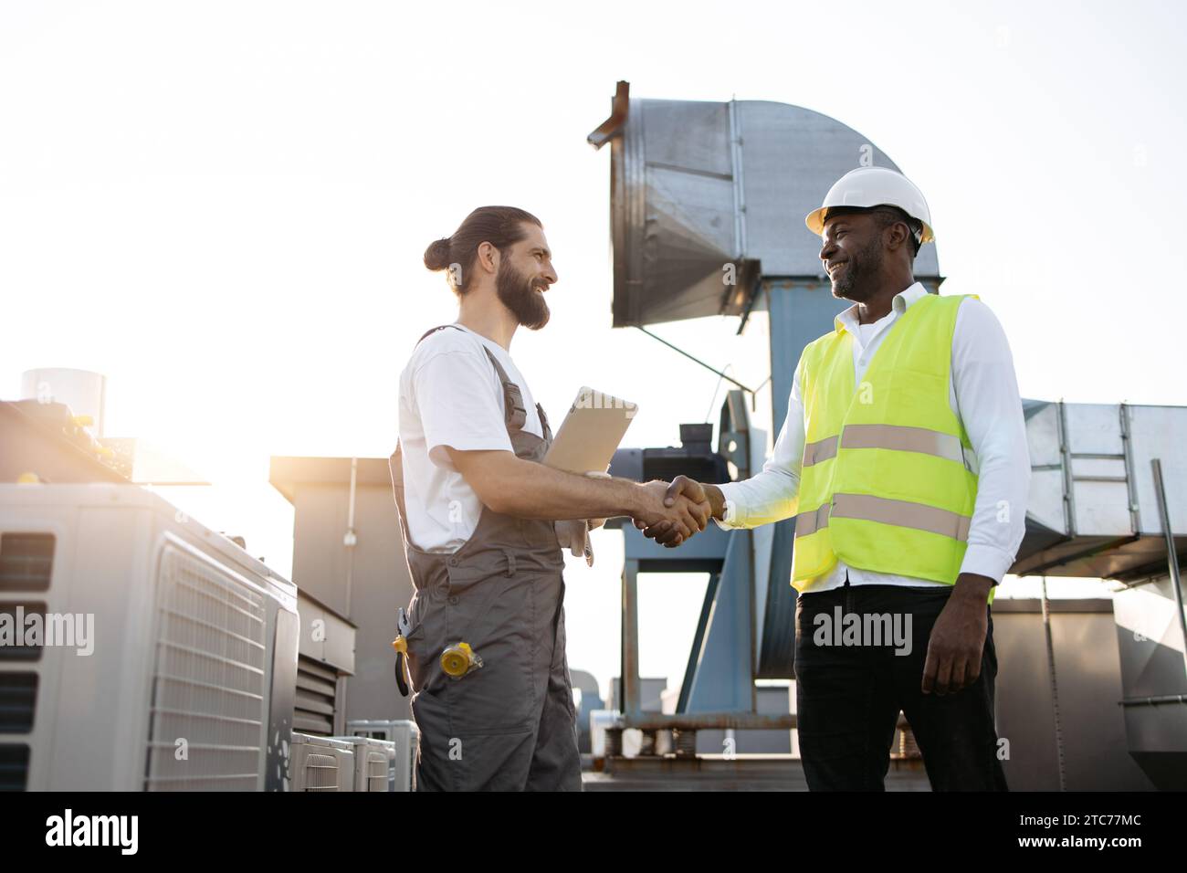 Multicultural workers smiling and shaking hands on roof Stock Photo - Alamy