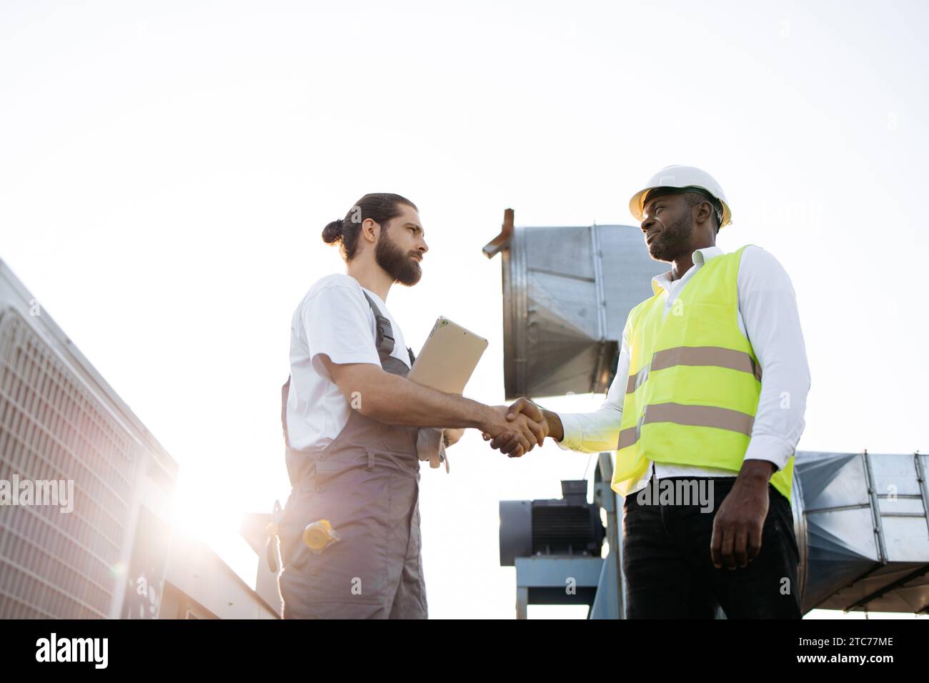 Multicultural workers smiling and shaking hands on roof Stock Photo - Alamy