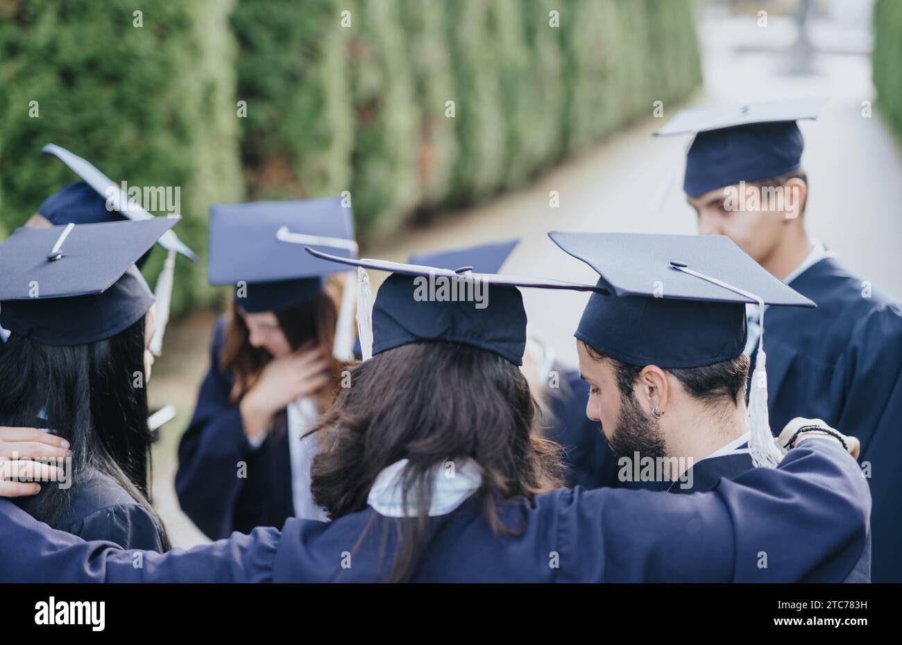 Graduating university students in gowns and caps stand in a park ...