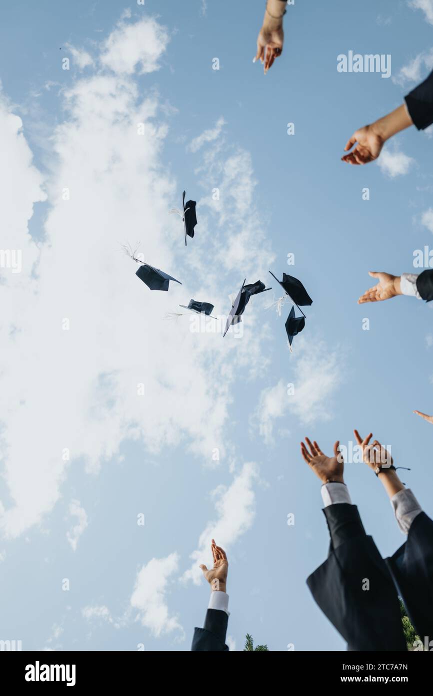 A group of happy students celebrating graduation in a park, throwing ...