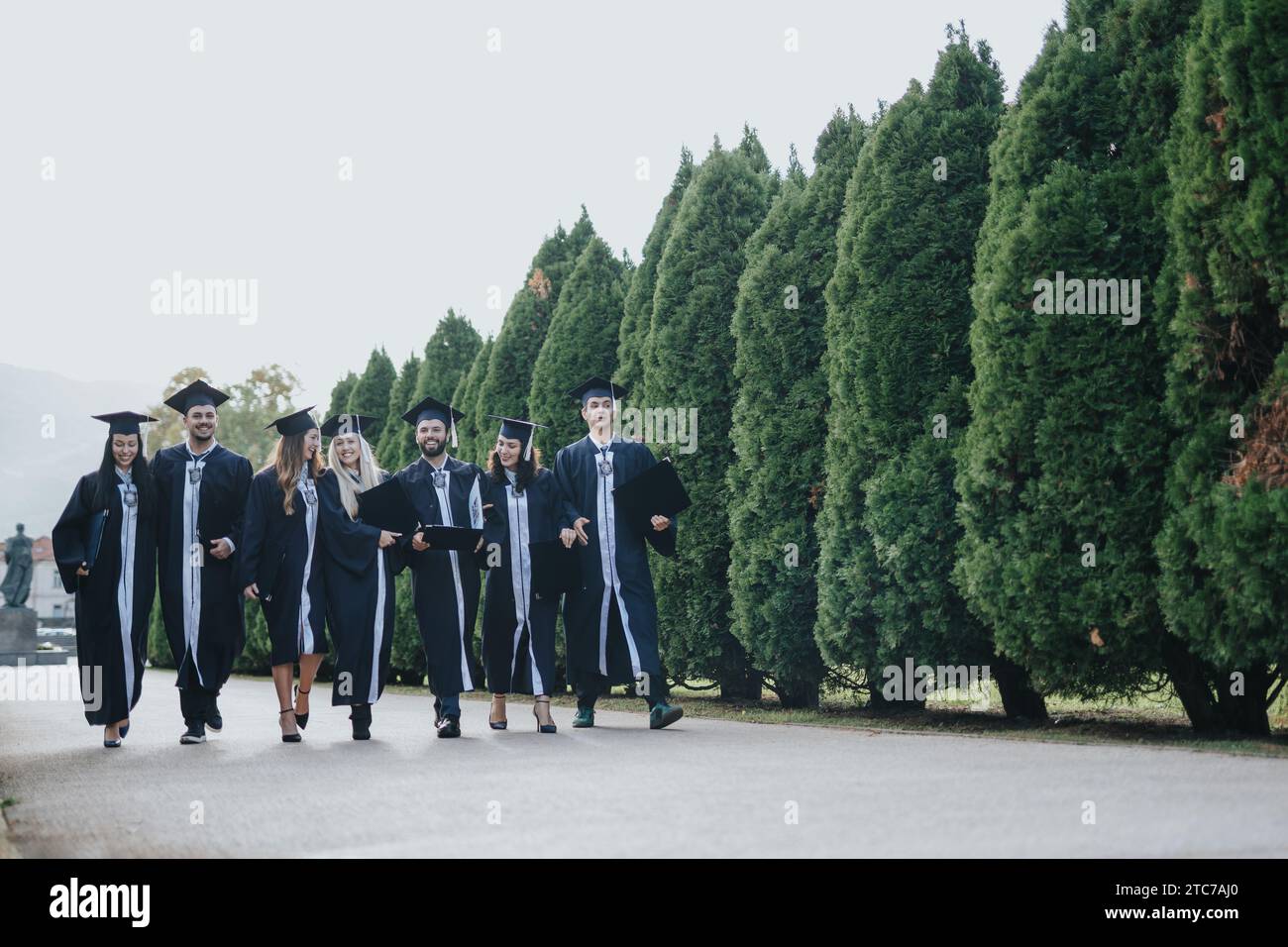 University students in graduation gowns celebrate in a sunlit park ...