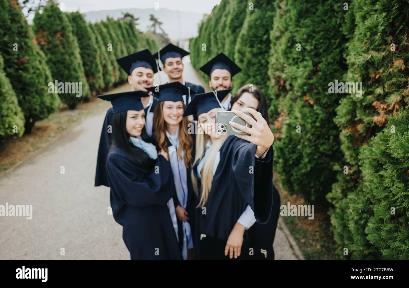 Friends celebrate graduation in a park wearing gowns and caps. They ...