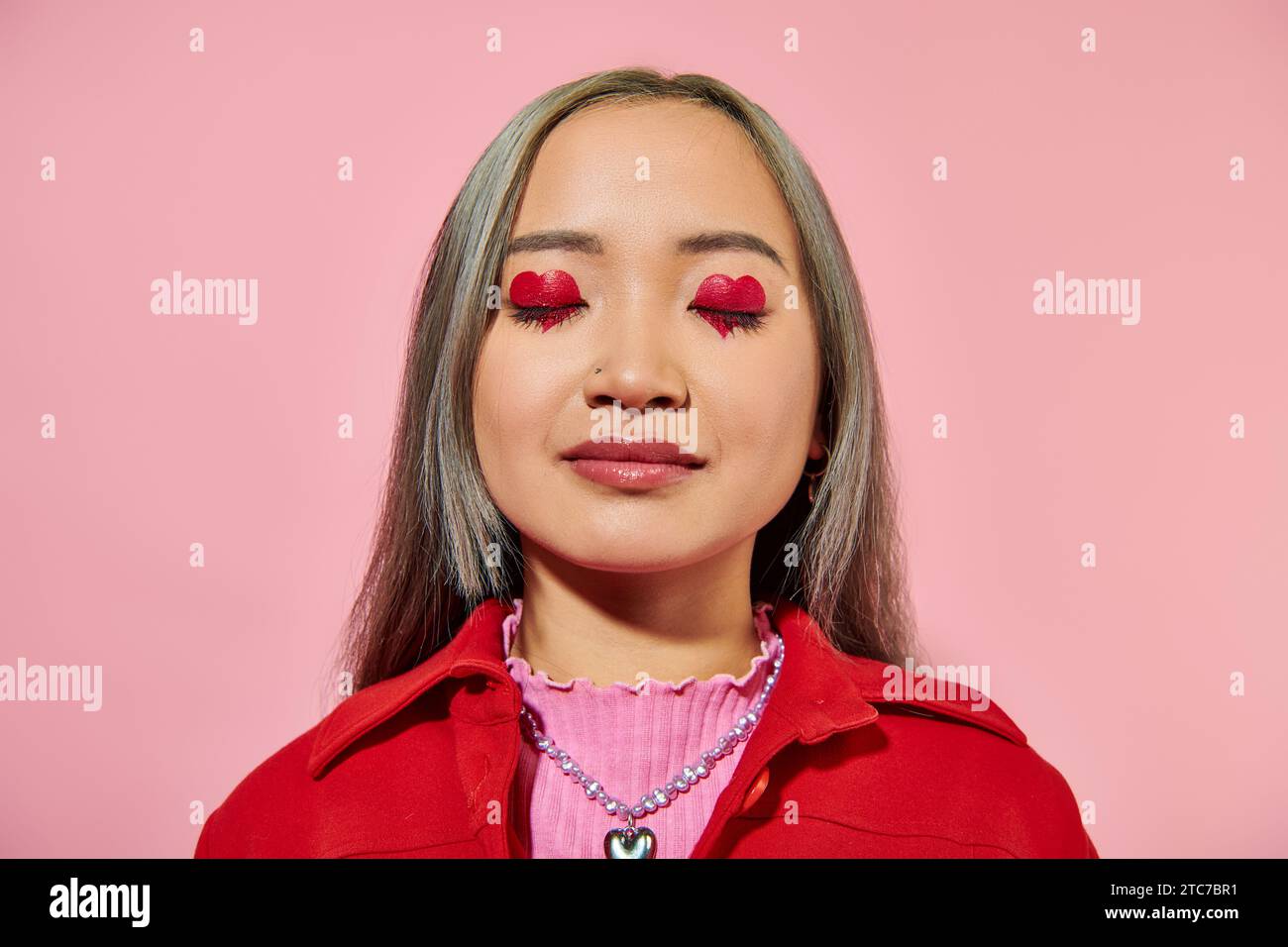 portrait of young asian woman with heart shaped eye makeup and dyed hair posing with closed eyes ...