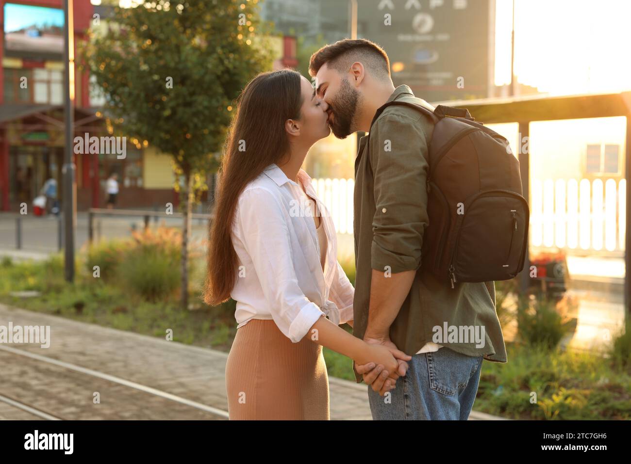 Long-distance relationship. Man with backpack kissing his girlfriend at railway station outdoors ...