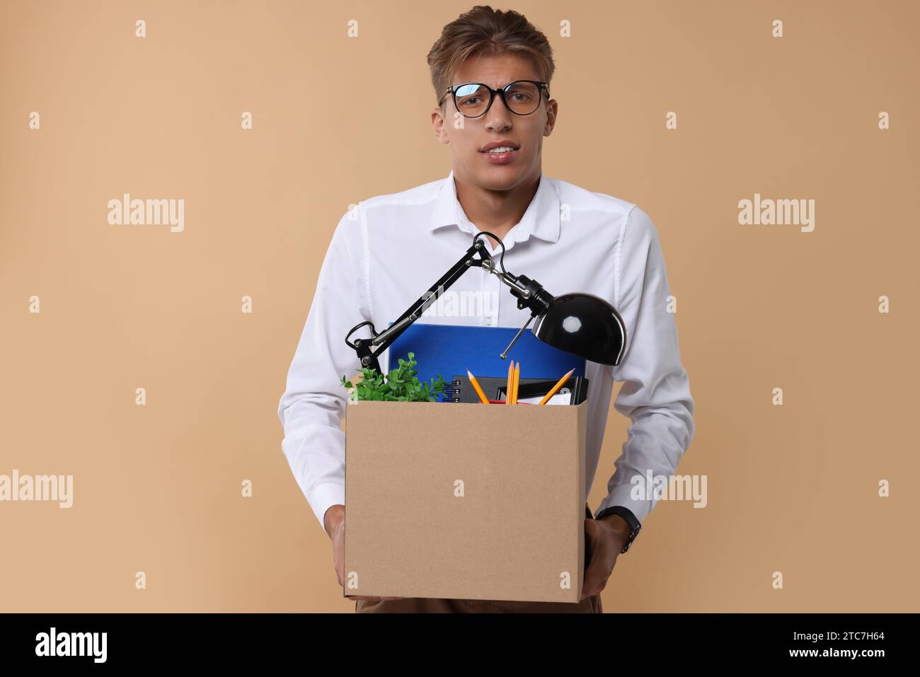 Unemployed young man with box of personal office belongings on beige ...