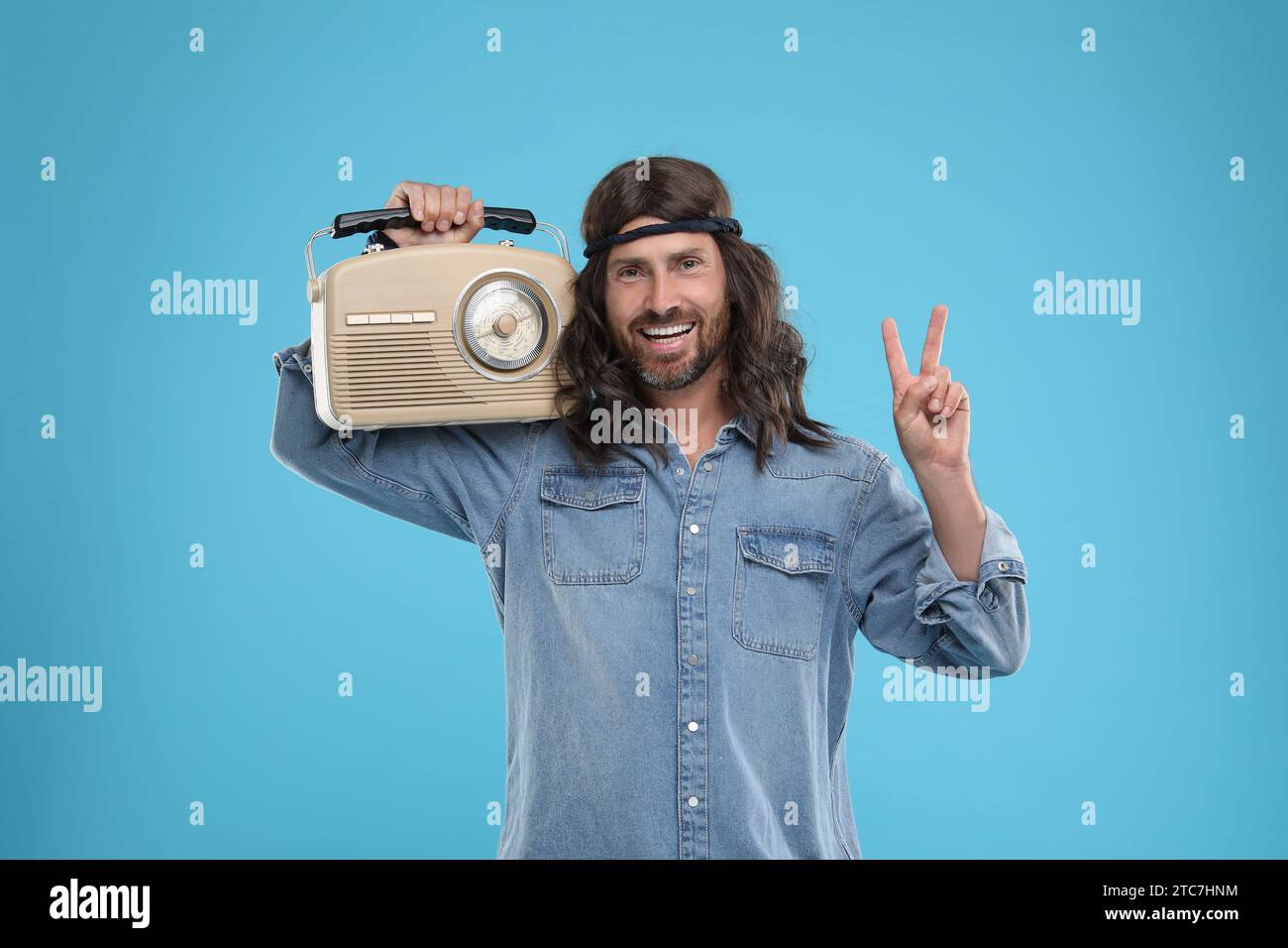 Stylish hippie man with retro radio receiver showing V-sign on light ...