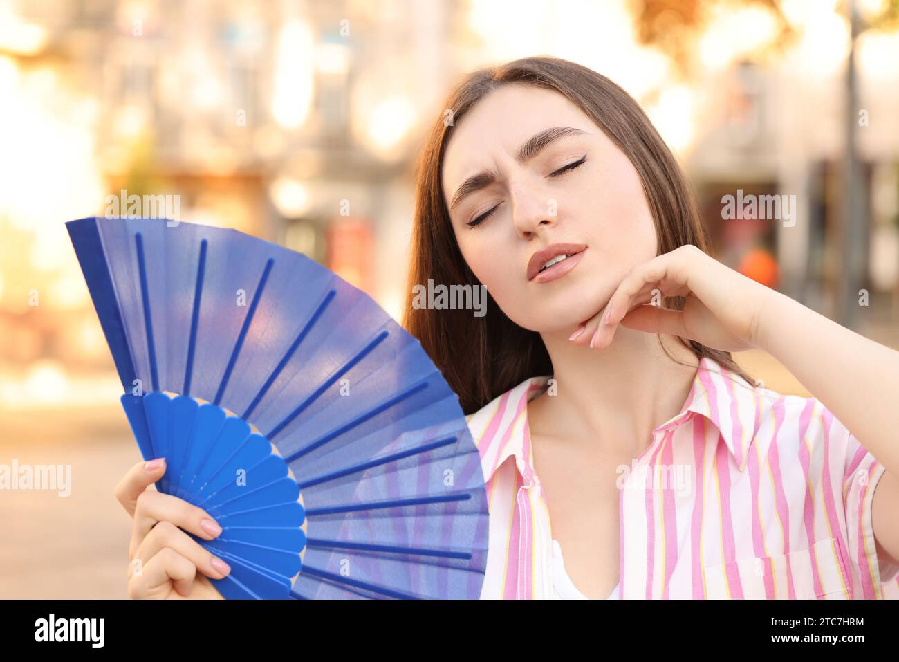 Woman with hand fan suffering from heat outdoors Stock Photo - Alamy