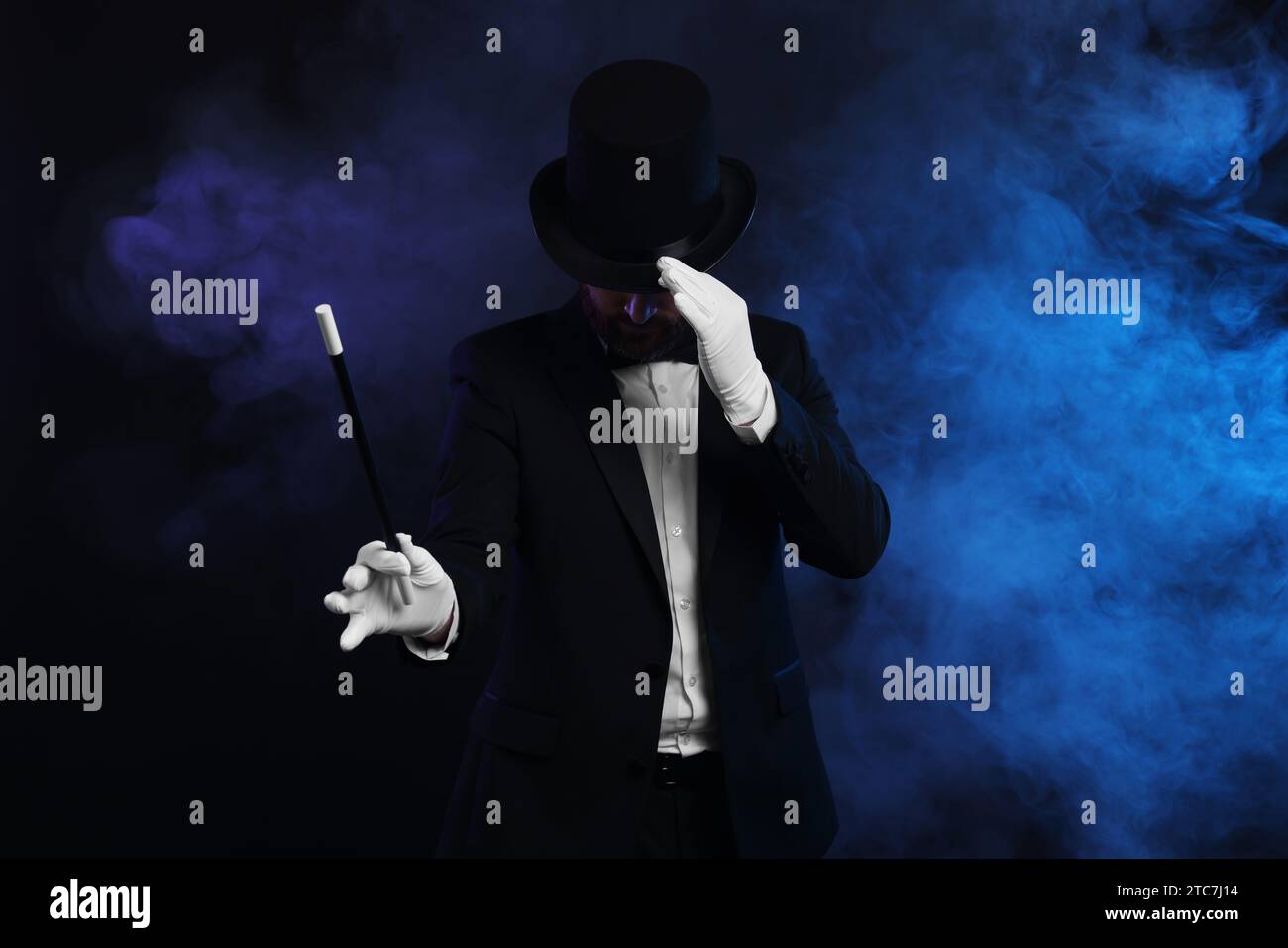 Magician holding wand in smoke on dark background Stock Photo - Alamy