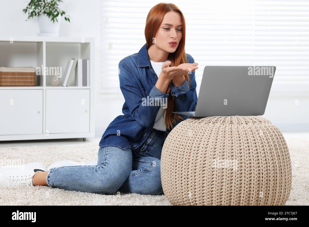 Woman blowing kiss during video chat via laptop at home. Long-distance ...