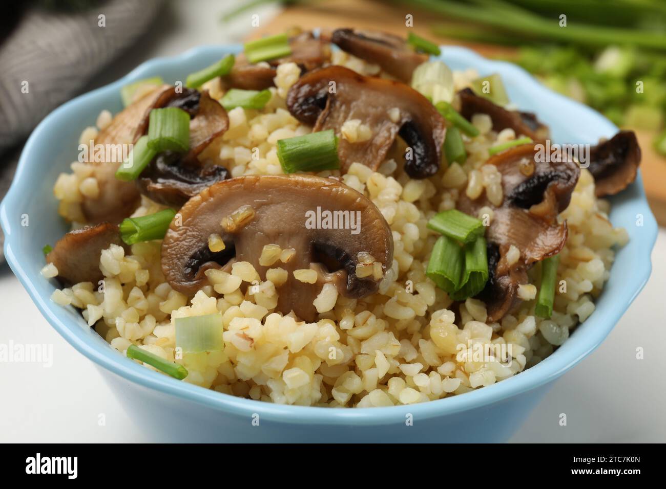 Delicious bulgur with mushrooms and green onion in bowl on table ...