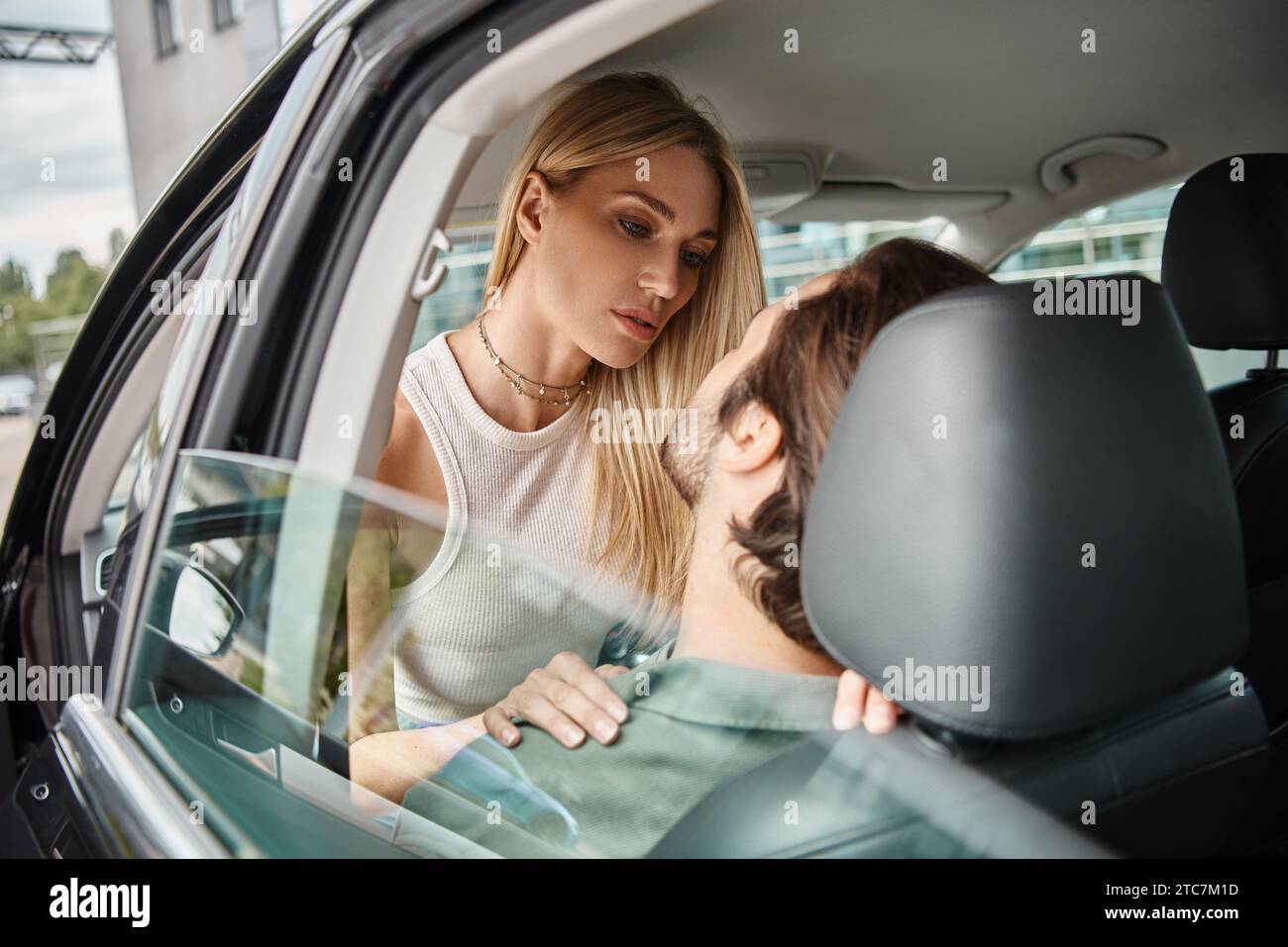attractive blonde woman seducing man sitting in modern car on urban ...