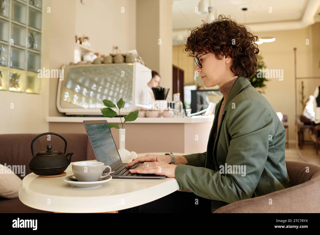 Female freelancer filling spreadsheet on her laptop while sitting at ...