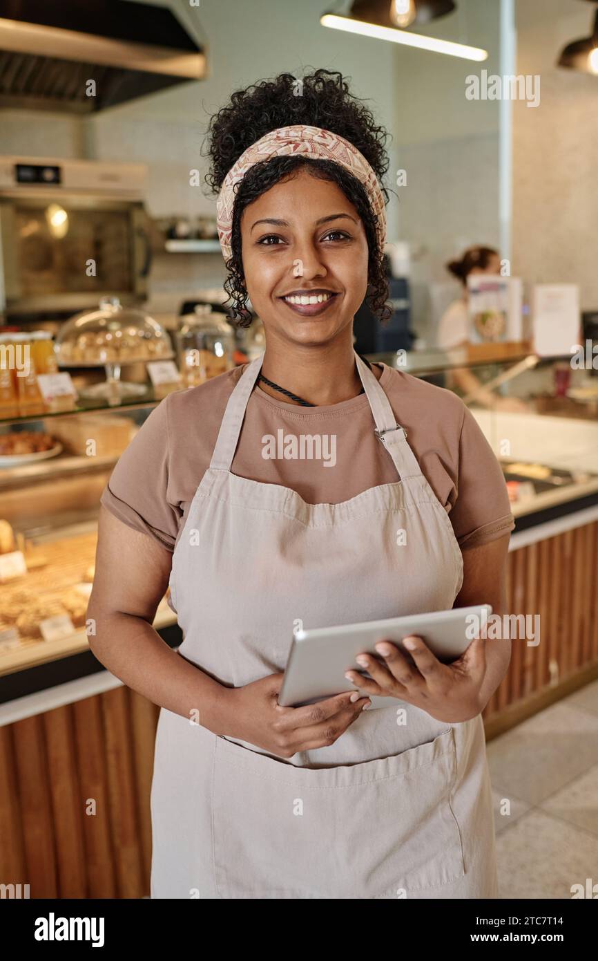 Local bakery waitress posing at her workplace holding digital tablet ...