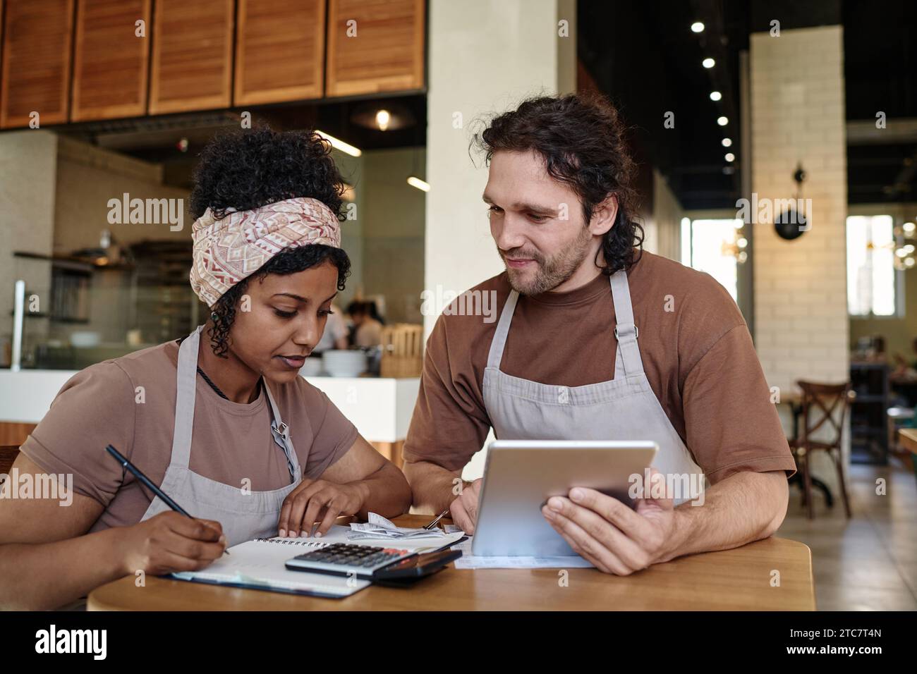 Two biracial eatery workers sitting over income calculation sitting at ...