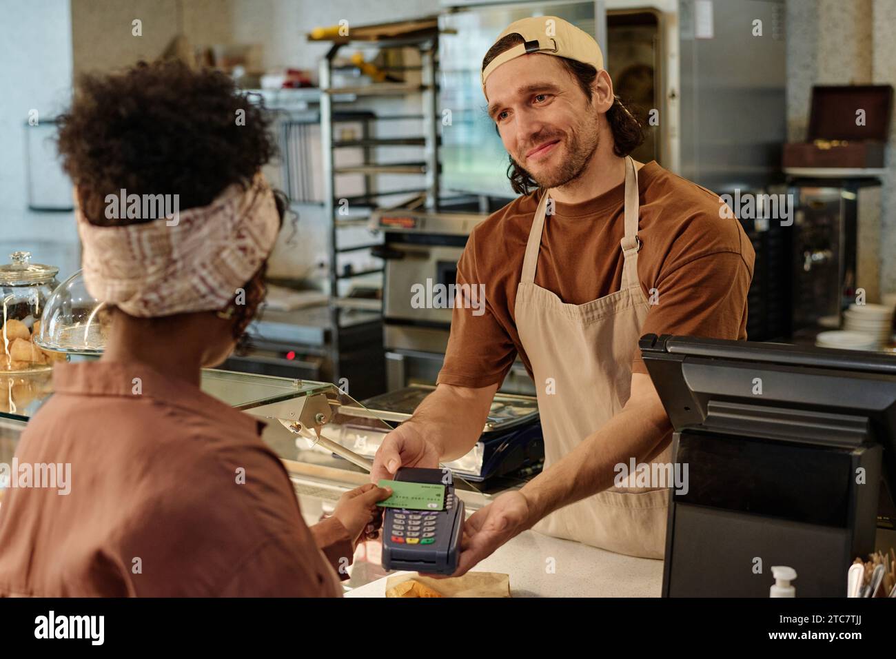 Medium shot of cheerful male cashier receiving cashless payment from ...