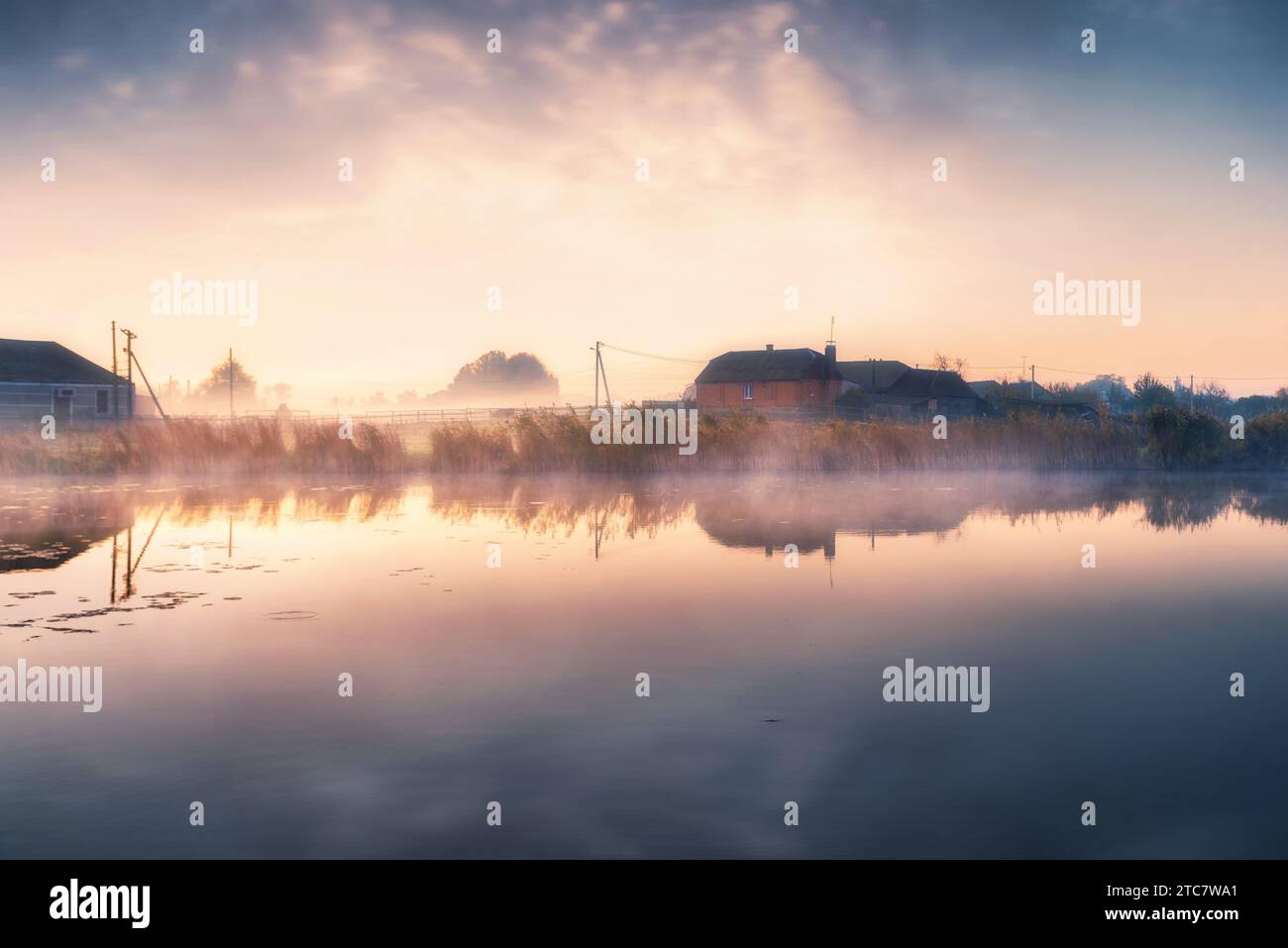Beautiful morning scene in tranquil village with a lake in the mist at ...