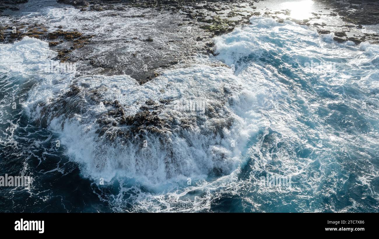 Foamy sea waves crashing onto rocky shore with sunlight reflecting on ...