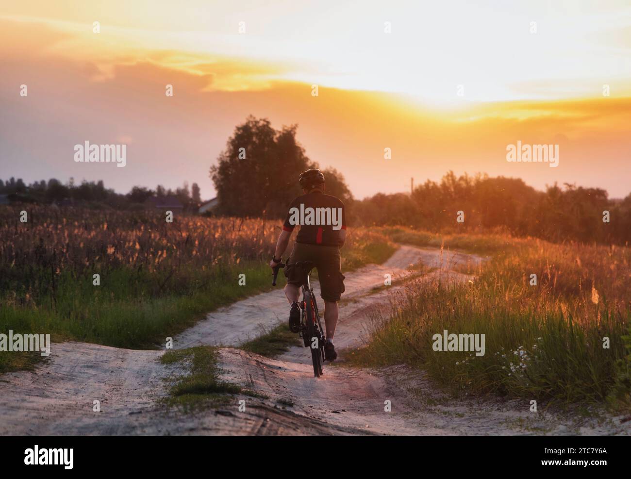 Cyclist riding a trail in a field on a gravel bike on a dramatic sunset ...