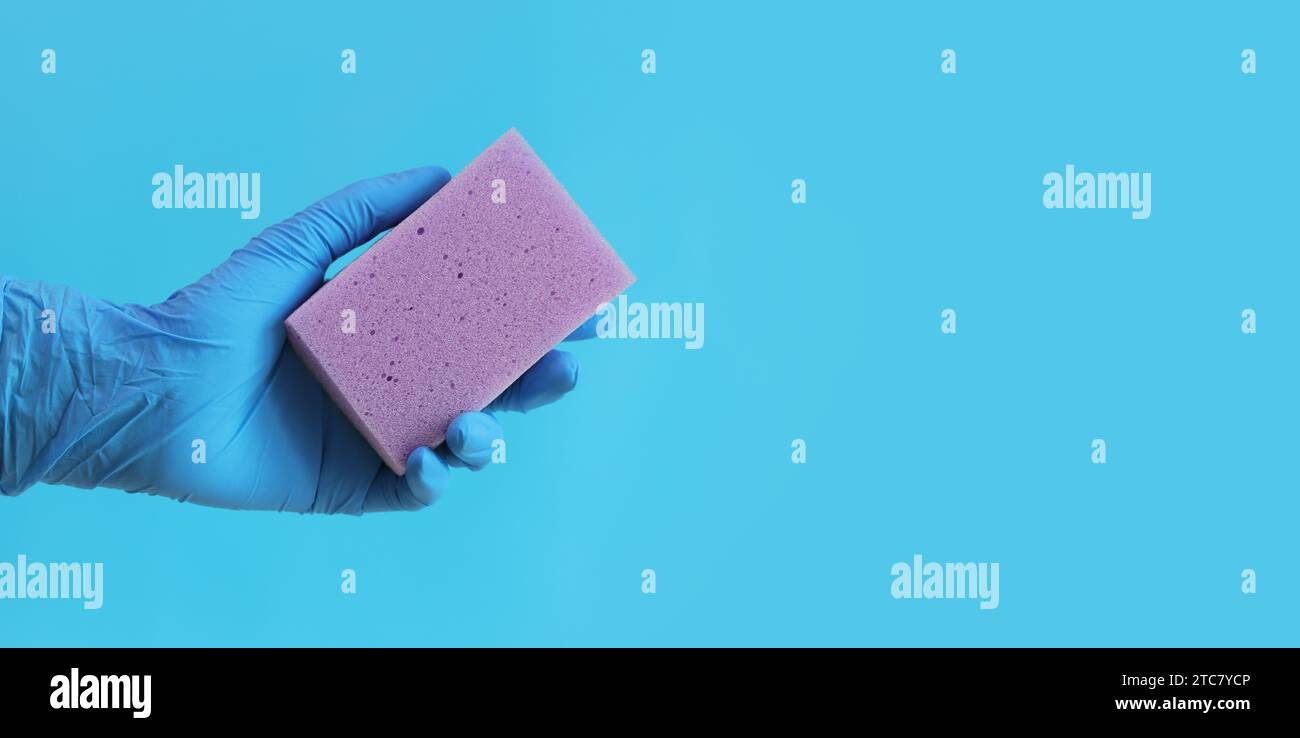 Purple dishwashing sponge in a woman's hand on a blue background. A ...