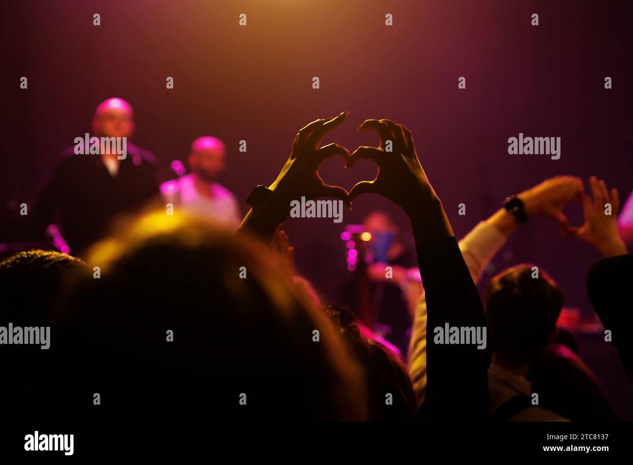 A crowd of people at a concert making heart shapes with their hands ...