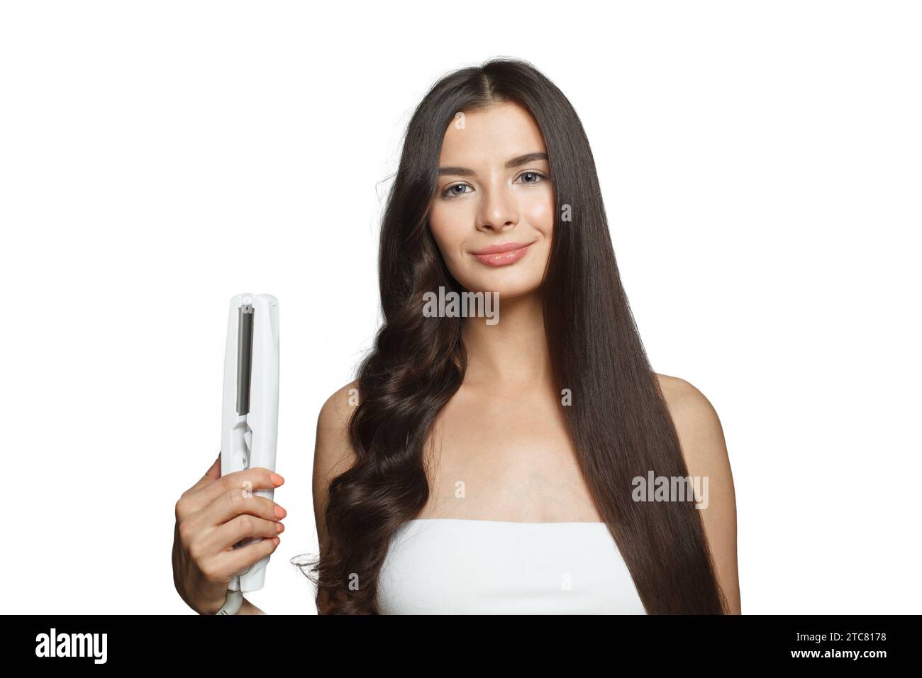Cheerful smiling woman using hair iron and straightening her long brown ...