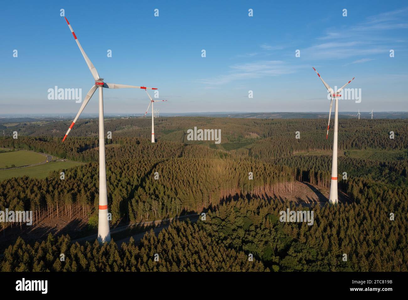 Wind turbines towering over a forested landscape with shadows cast by ...
