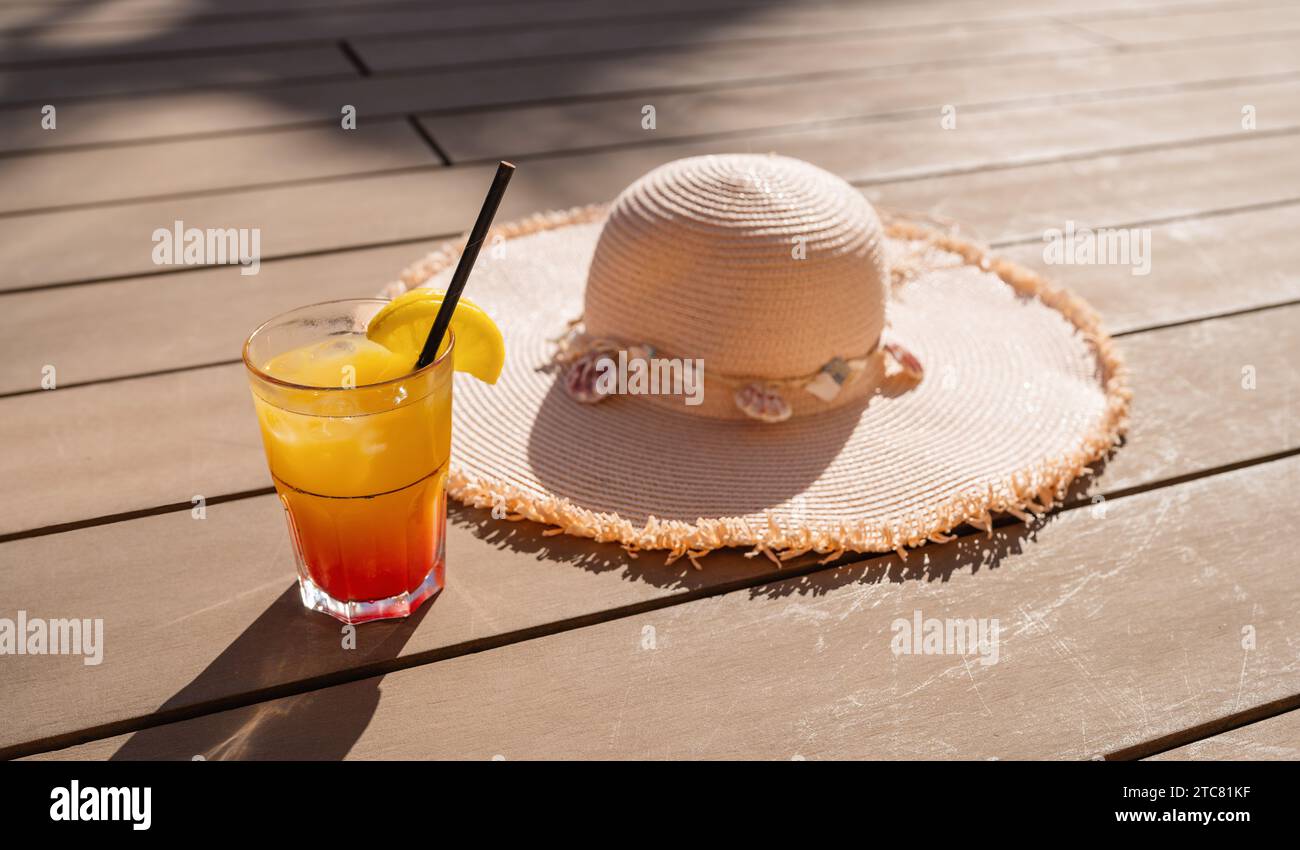 Cocktail with orange slice and straw next to a straw hat on a wooden ...