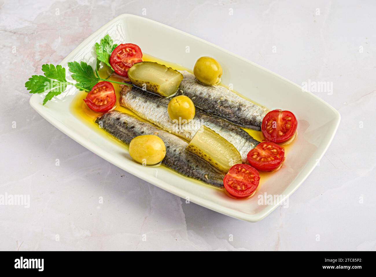 A white ceramic plate filled with marinated sardines and fresh garnish ...