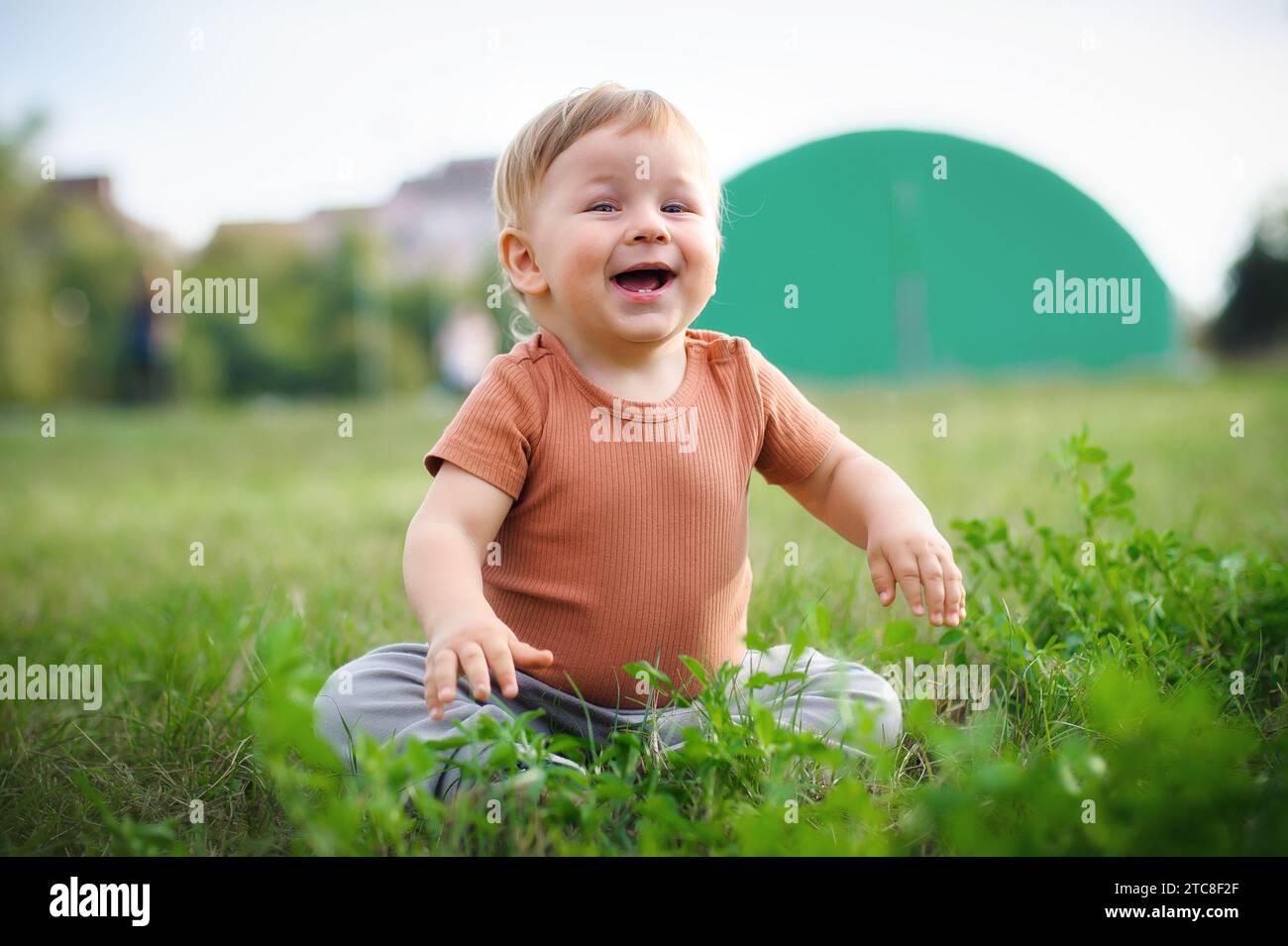 Cute laughing baby having fun sitting on grass in sunshine day. Summer time, happy baby Stock ...