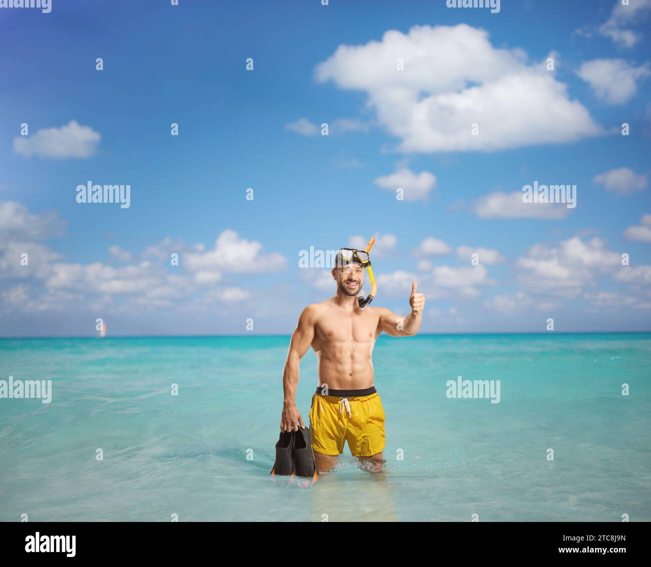 Guy standing into the sea with a diving mask and fins and showing ...