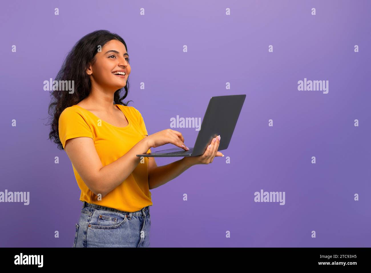 Positive young hindu lady using computer on purple background Stock ...