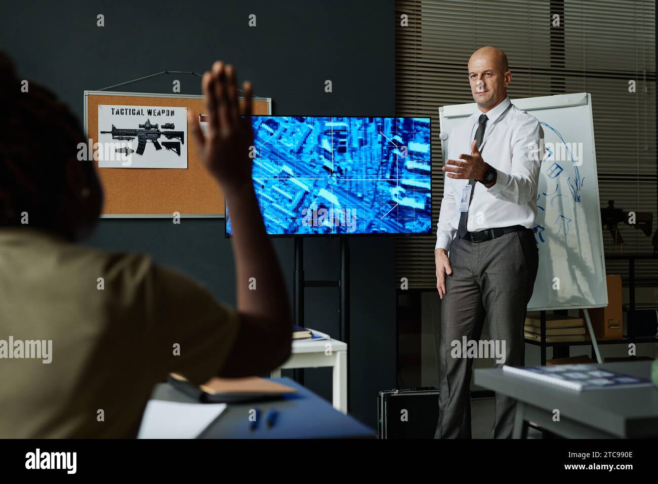Bald mature officer pointing at student raising her hand at lesson of ...