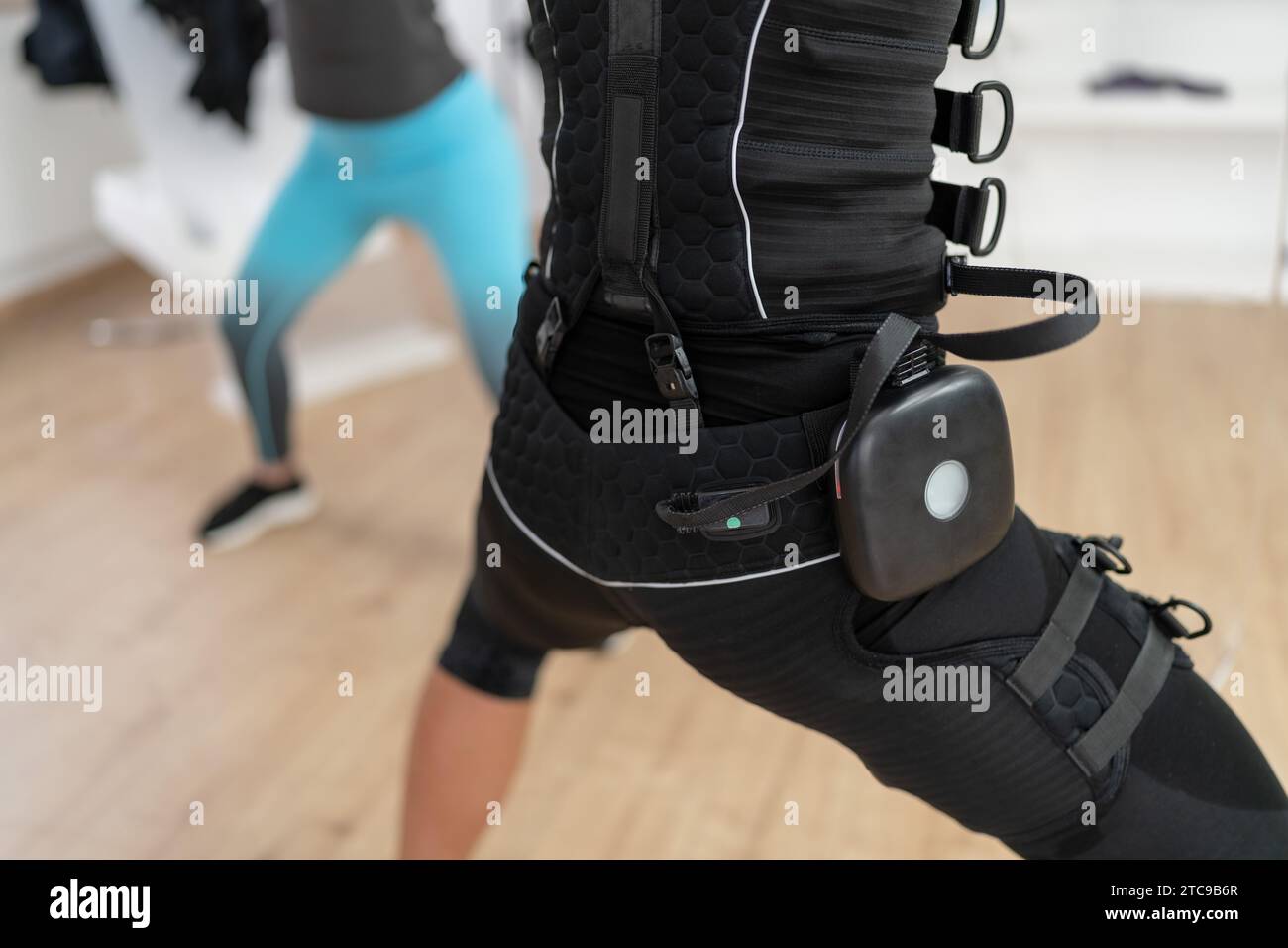 Two women performing squats in a gym, one wearing an EMS training suit ...